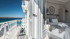 Quarto com cama, vista para o mar e varanda com grades brancas.