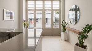 Uma área de recepção moderna com entrada por porta de vidro, balcão de atendimento e plantas em vasos.