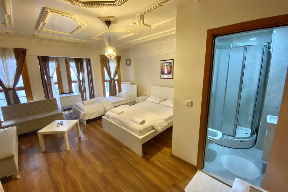 Quarto de hotel com duas camas, um sofá, uma mesa pequena e área de chuveiro.