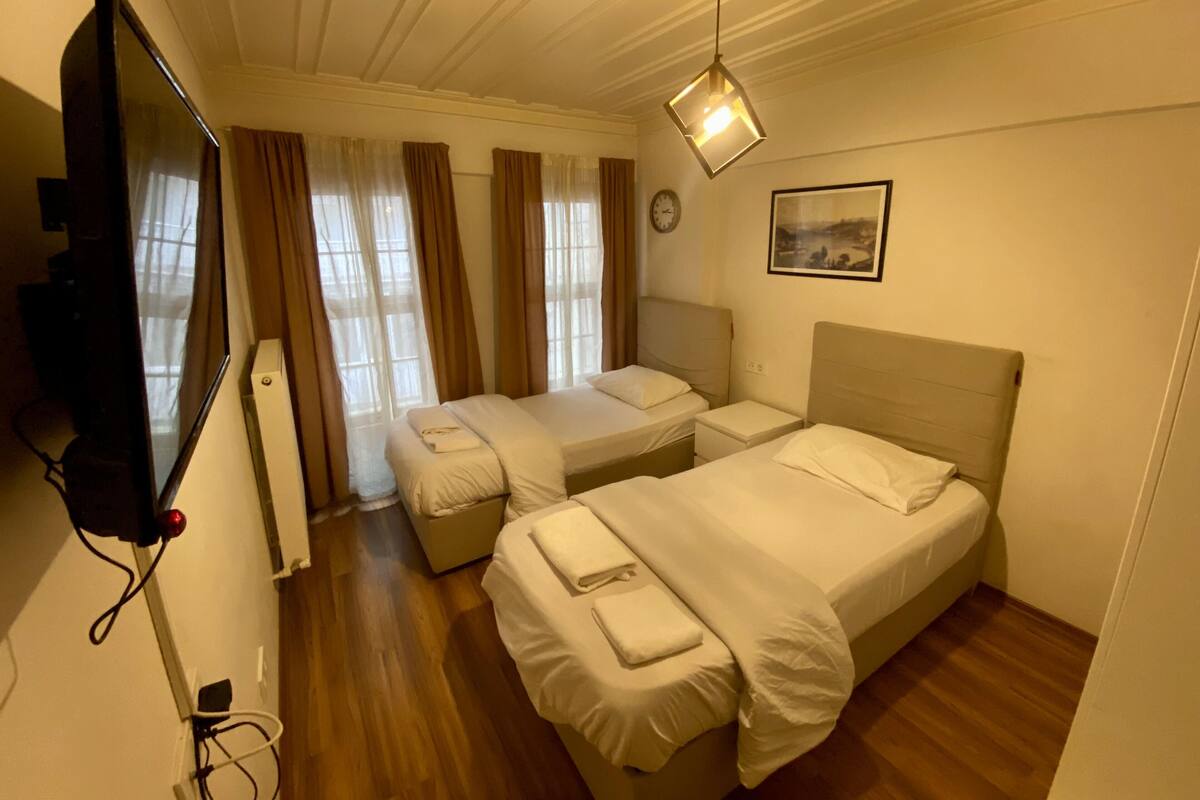 Quarto de hotel com duas camas, uma TV de tela plana, um relógio e um quadro na parede.