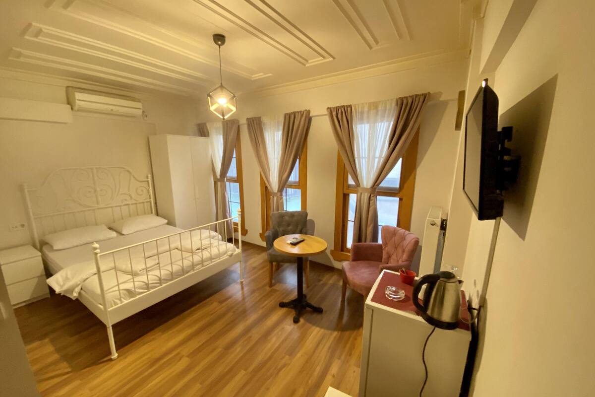 Quarto de hotel com cama, cadeira, mesa, televisão e janela com cortinas.