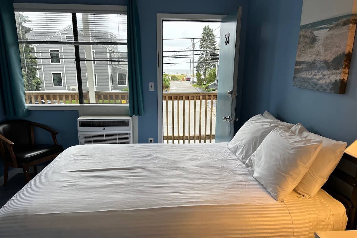 Quarto com cama, cadeira, ar condicionado e vista para a varanda.