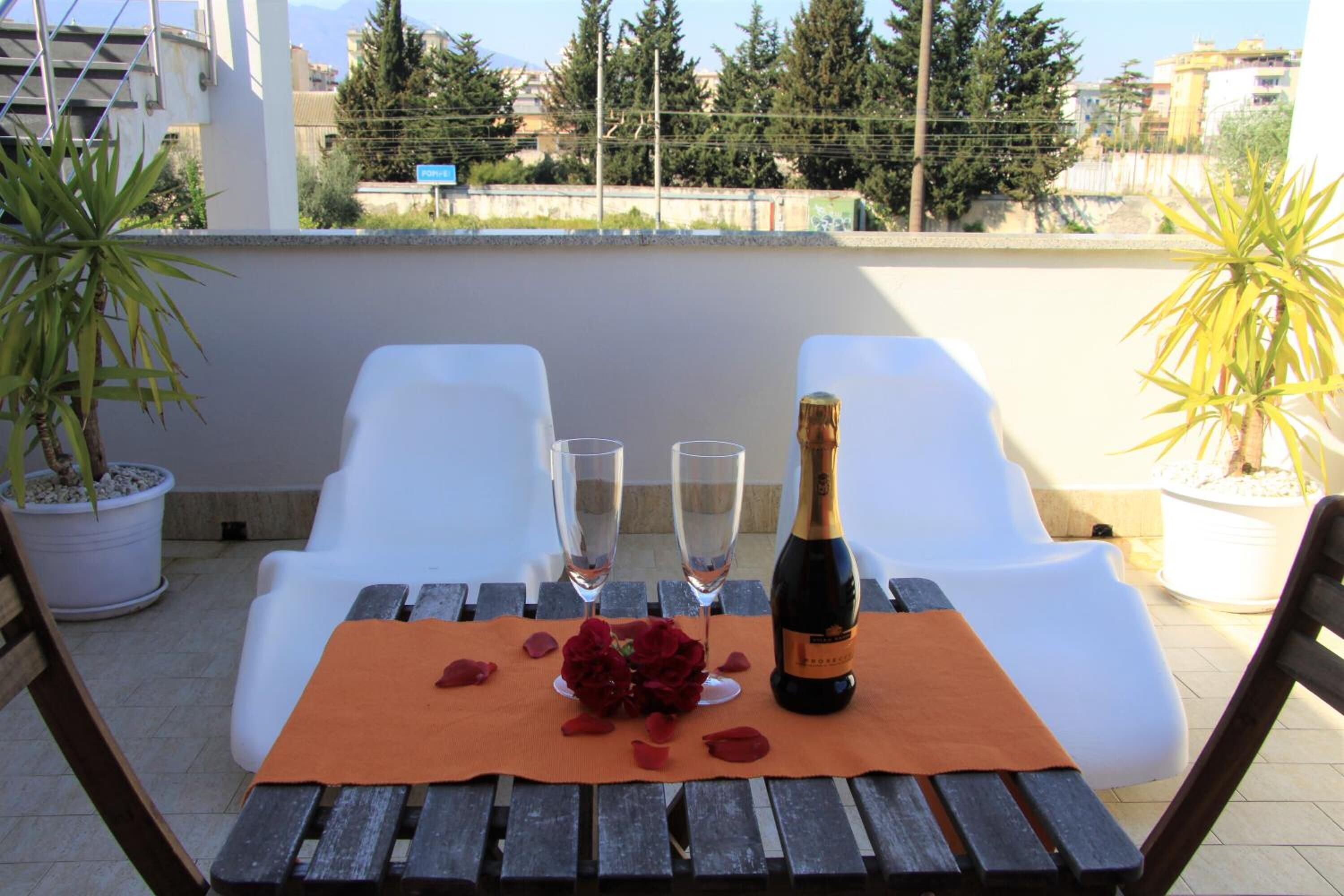 Um terraço com uma mesa posta para dois, com uma garrafa de champanhe, duas taças e pétalas de rosa.