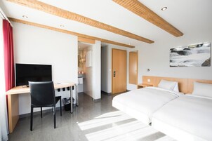 Quarto de hotel com cama, escrivaninha e cadeira, televisão e um quadro na parede.