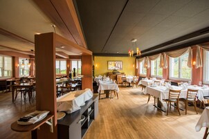 Um restaurante com várias áreas de refeição, pisos de madeira e grandes janelas que permitem entrada de luz natural.