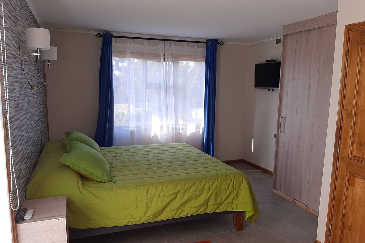 Um quarto com cama, televisão, guarda-roupa e janela com cortinas.