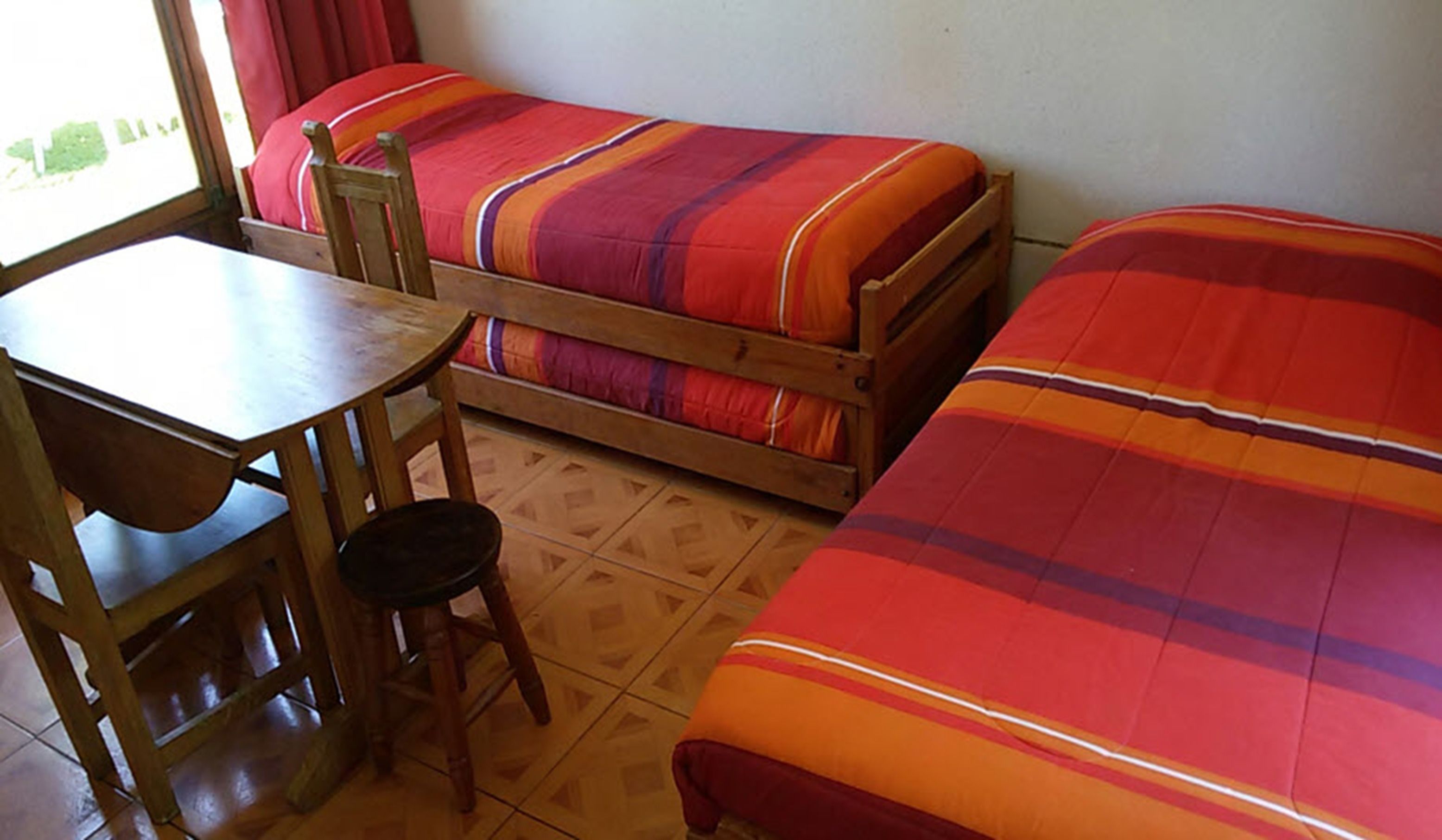 Quarto de dormitório com duas camas de solteiro, uma escrivaninha de madeira e uma cadeira.