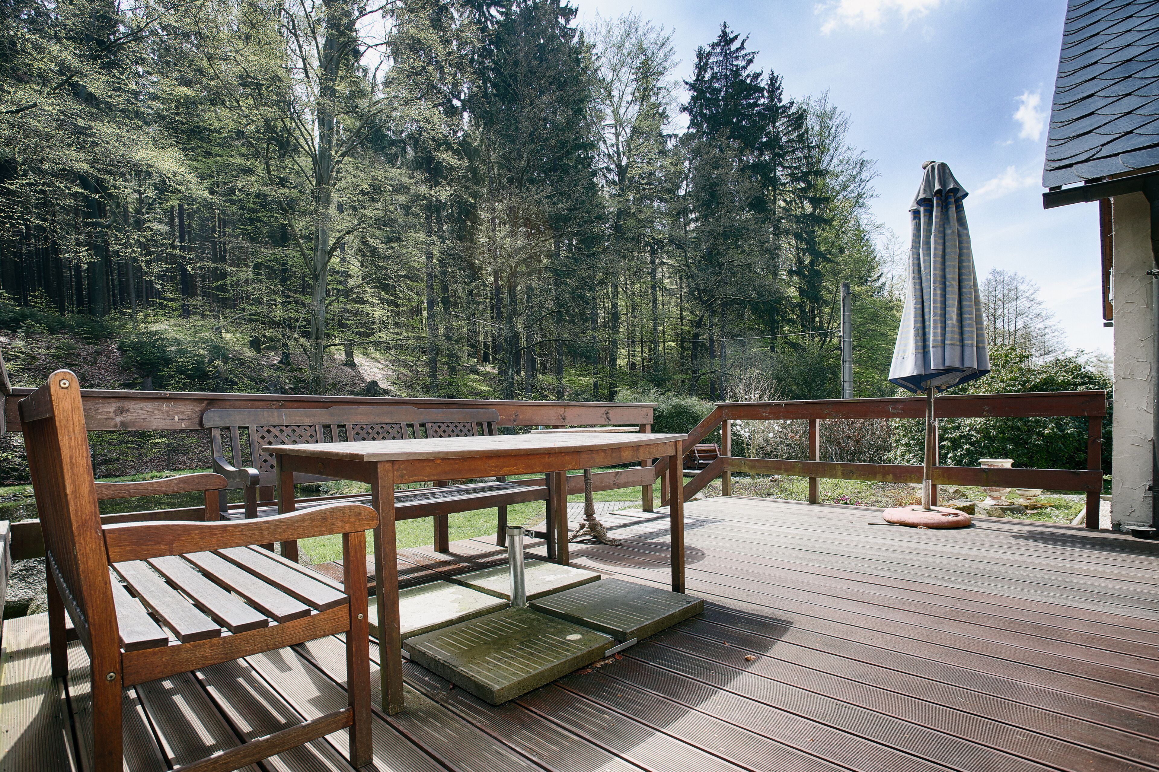 Um deck de madeira com mesa para piquenique e bancos, cercado por uma área arborizada.