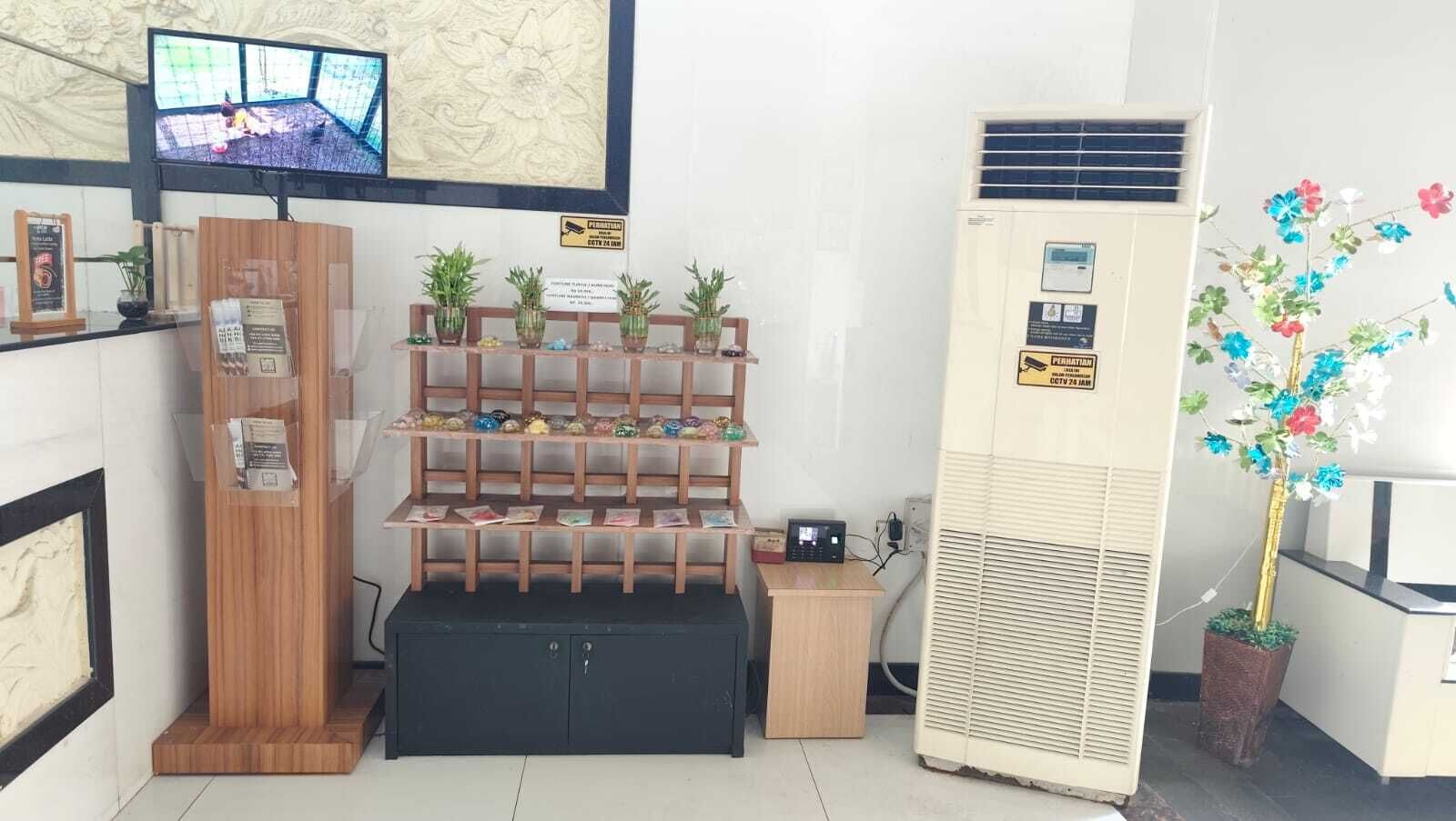 Uma área de recepção com uma mesa de madeira, uma estante com objetos decorativos, uma televisão e uma câmera de segurança.