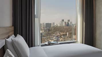 Quarto de hotel com uma cama grande, vista para a cidade através de uma janela e cortinas.