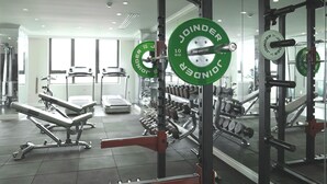 Uma academia com equipamentos de musculação, bancos e um espelho grande na parede.