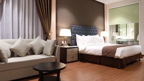 Quarto de hotel com cama, sofá, mesa de cabeceira, luminária e mesa redonda.
