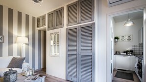 Uma sala de estar moderna com sofá, mesa de centro e lustre. Uma cozinha visível através de uma porta aberta.