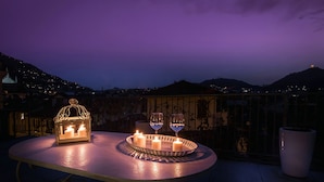 Mesa com velas e copos em terraço com vista para a cidade ao entardecer.