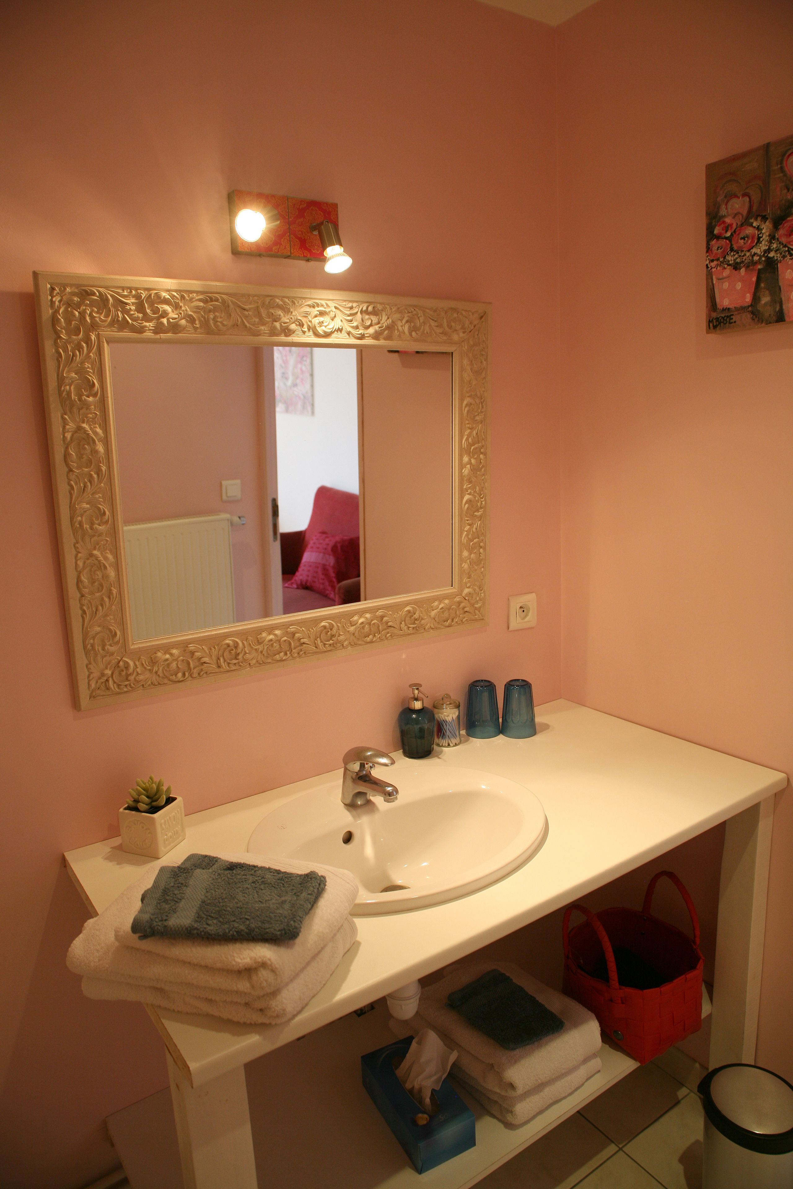 Uma casa de banho com uma pia branca, um espelho grande e ornamentado e uma parede cor-de-rosa.