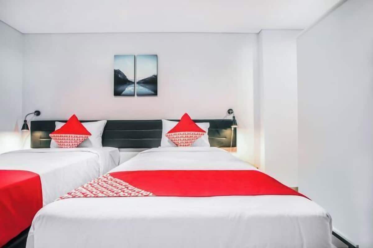 Quarto de hotel com duas camas, um cobre-leito vermelho e branco e uma obra de arte pendurada na parede.