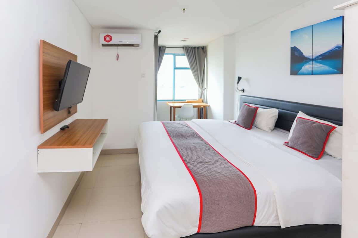 Quarto de hotel moderno com uma cama grande, televisão montada, escrivaninha e janela com cortinas.