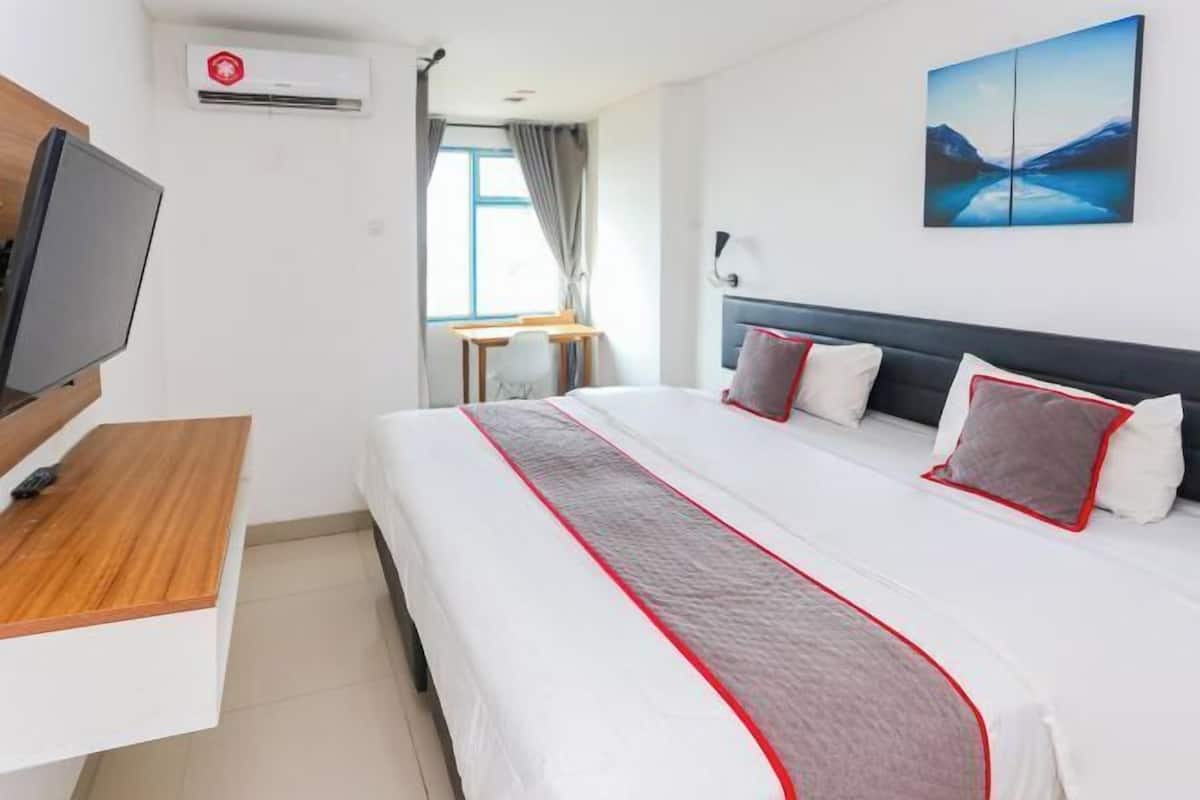 Quarto de hotel com cama, escrivaninha, televisão e um quadro na parede.