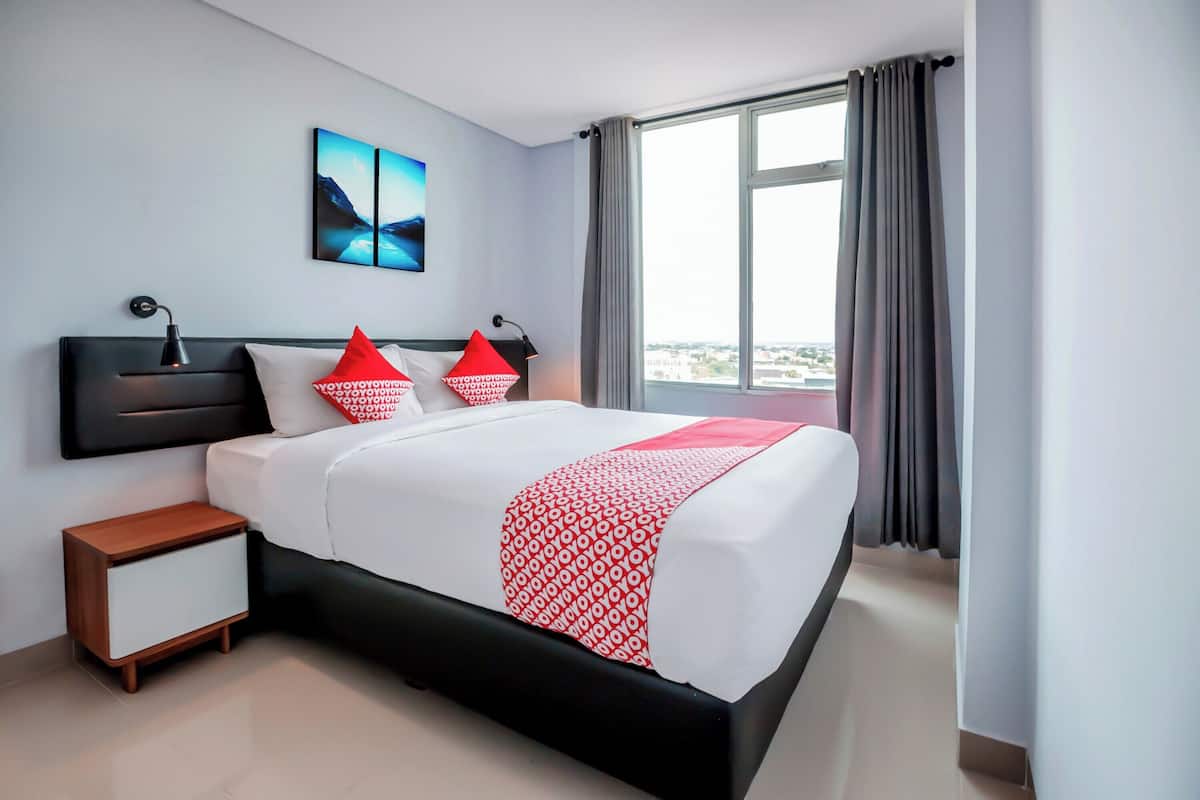 Quarto de hotel moderno com uma cama grande, mesa de cabeceira, luminária fixada na parede e vista para a cidade pela janela.