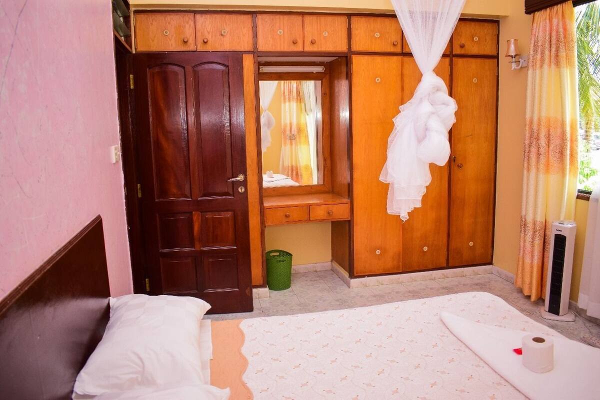 Quarto com cama, guarda-roupa, janela com cortinas e mesa de cabeceira.