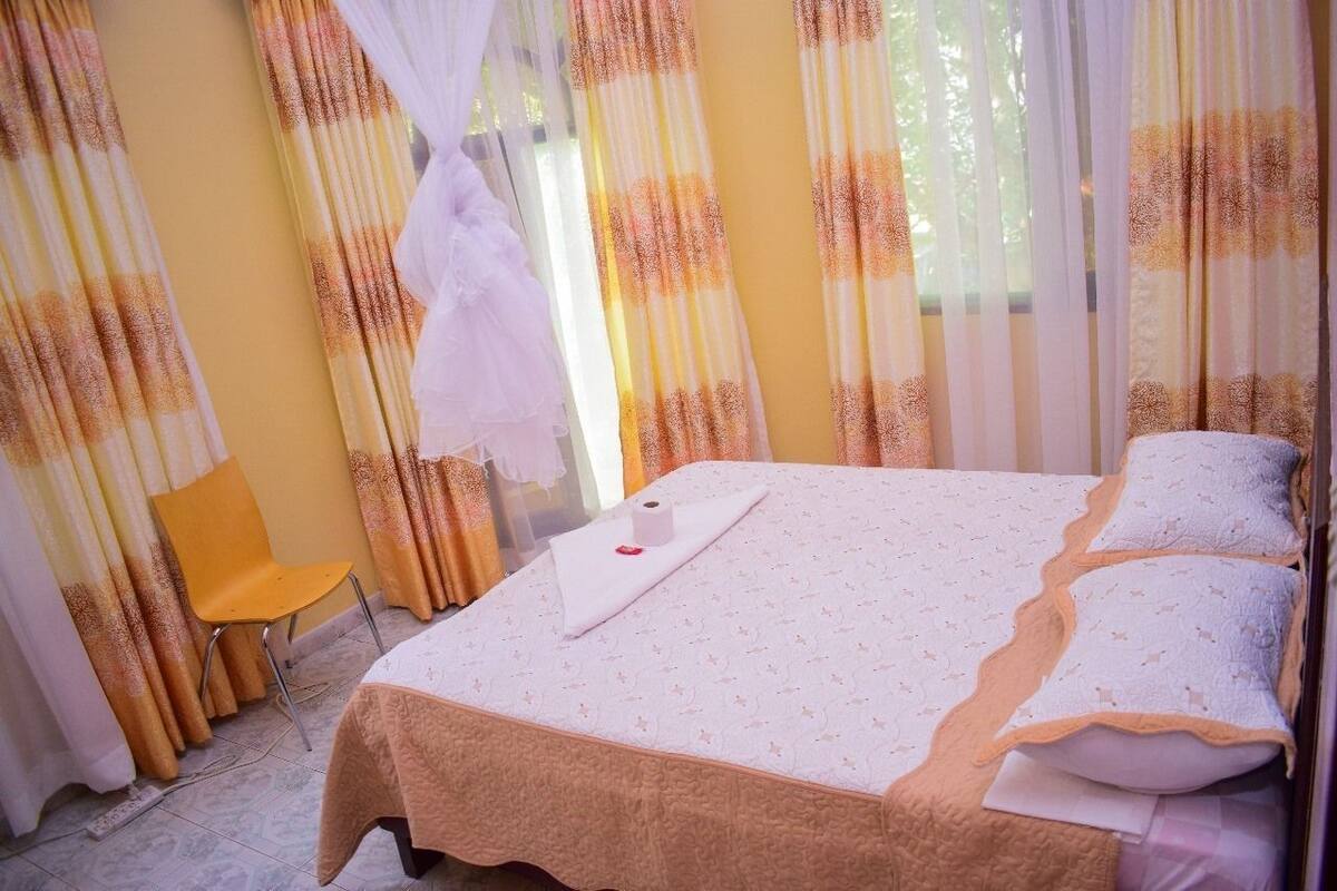 Quarto de hotel com cama, cortinas, uma cadeira e janela.