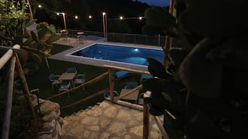 Uma piscina com um deck de pedra, rodeada por uma cerca de madeira e luzes de corda.