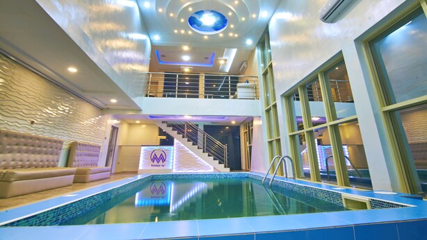 Piscina interior moderna com teto de vidro, varanda no segundo andar e área de estar confortável.
