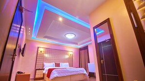 Quarto de hotel moderno com uma cama grande, cabeceira embutida e iluminação azul de LED no teto.