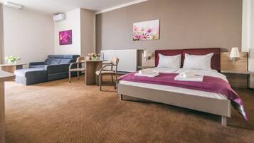 Quarto de hotel com uma cama grande, um sofá, uma pequena mesa com cadeiras, um radiador e obras de arte nas paredes.