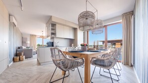 Uma cozinha moderna com  área de refeições, com uma mesa de madeira, cadeiras de vime e luminárias pendentes.
