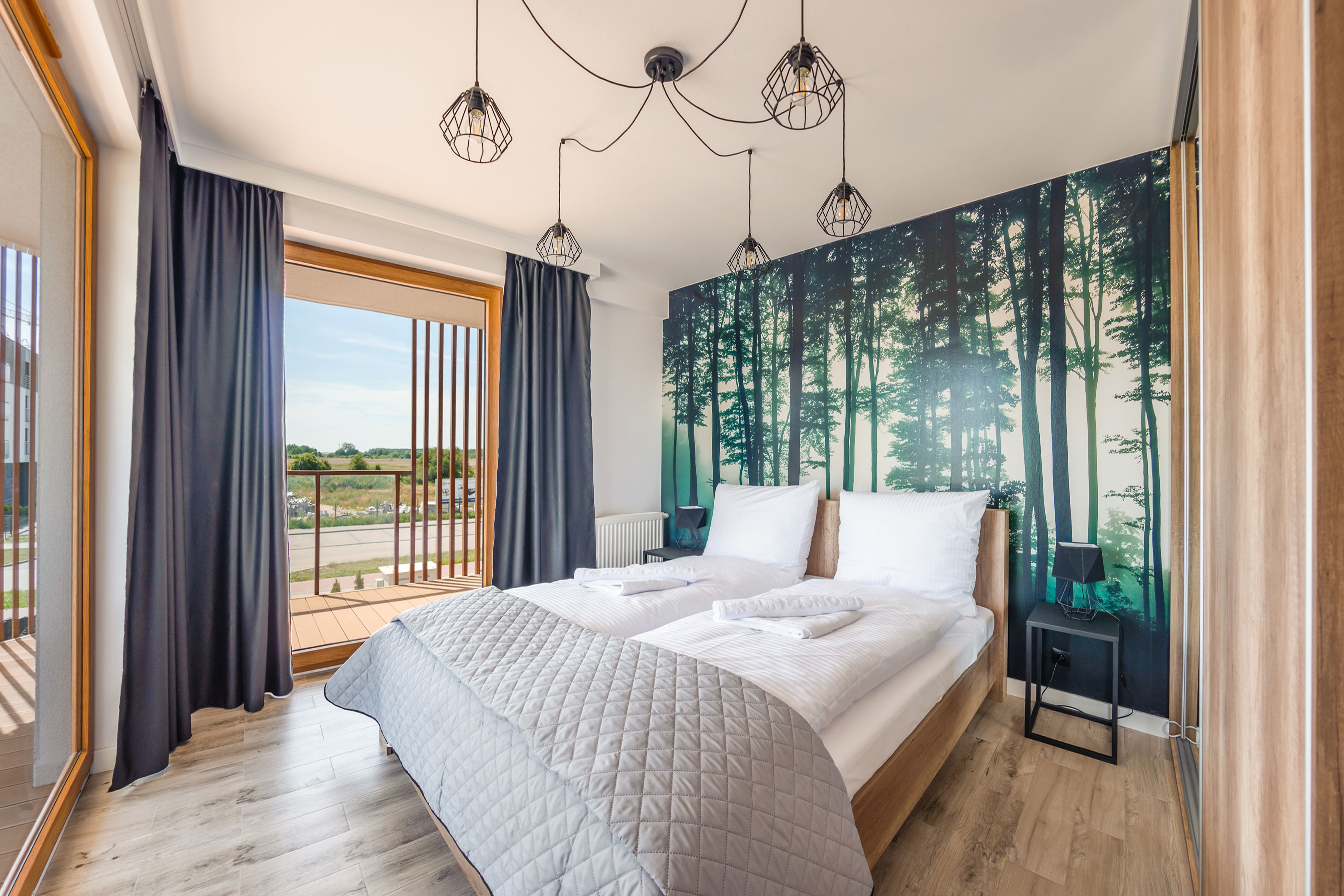Quarto com uma cama grande, vista para o exterior e um mural temático de floresta.