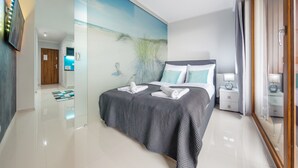 Quarto de hotel moderno com uma cama grande, mesa de cabeceira, TV e parede divisória de vidro.