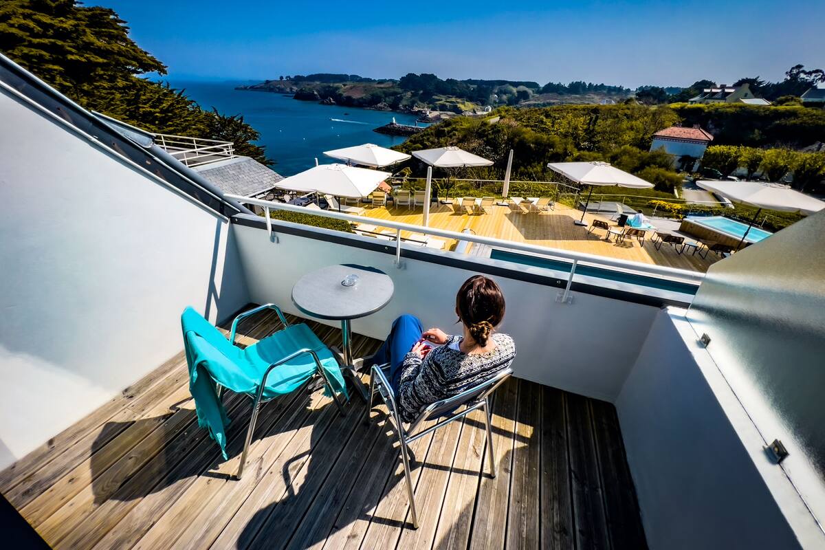 Varanda com vista para o mar, deck de madeira e área de estar ao ar livre com guarda-sóis.