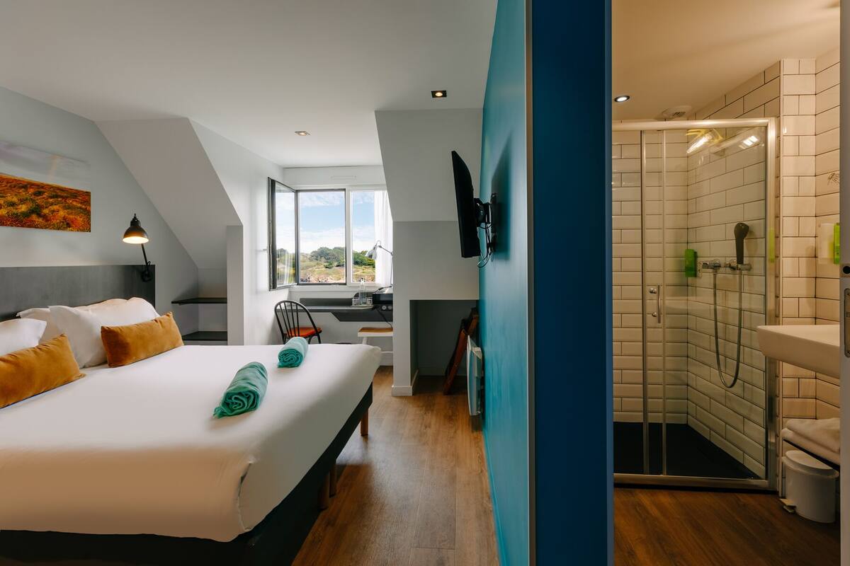 Quarto de hotel moderno com uma cama grande, uma escrivaninha e vista para o exterior.