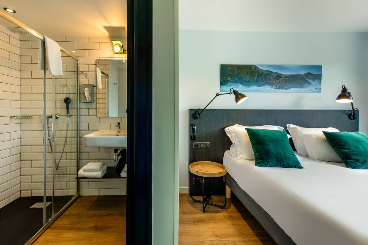 Quarto de hotel moderno com chuveiro, pia e cama com travesseiros verdes.