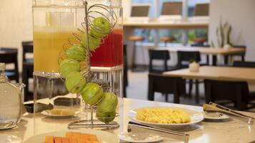 Um buffet de café da manhã com diversas frutas, um jarro de suco de laranja e um copo de suco vermelho.