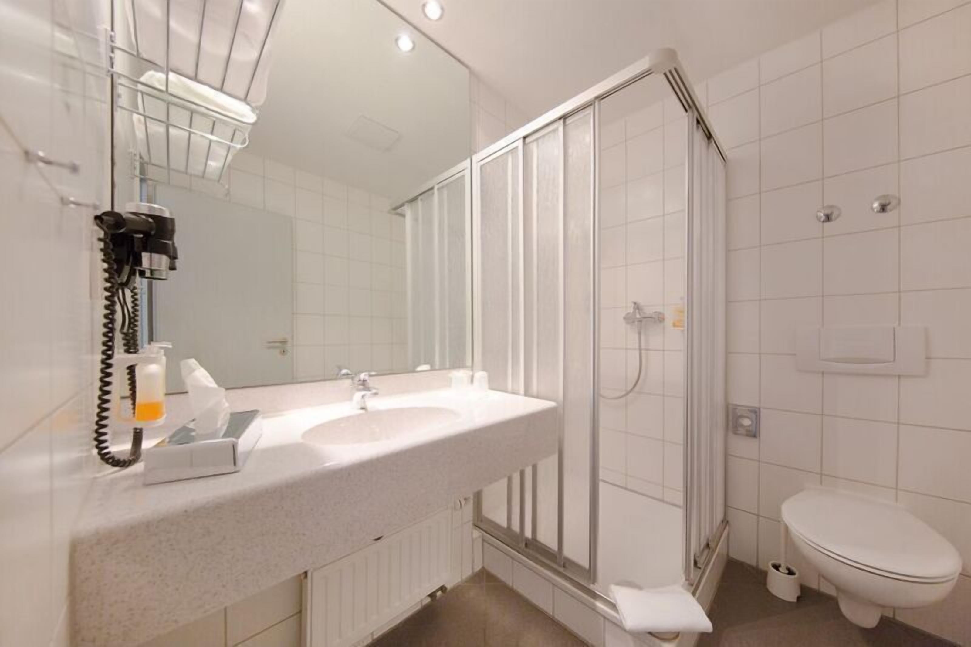 Uma casa de banho moderna com chuveiro de cabine de vidro, lavatório branco com espelho e sanita.