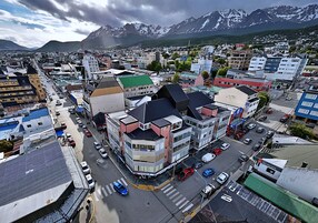 Um edifício de vários andares com telhado verde, situado numa vila com montanhas ao fundo.