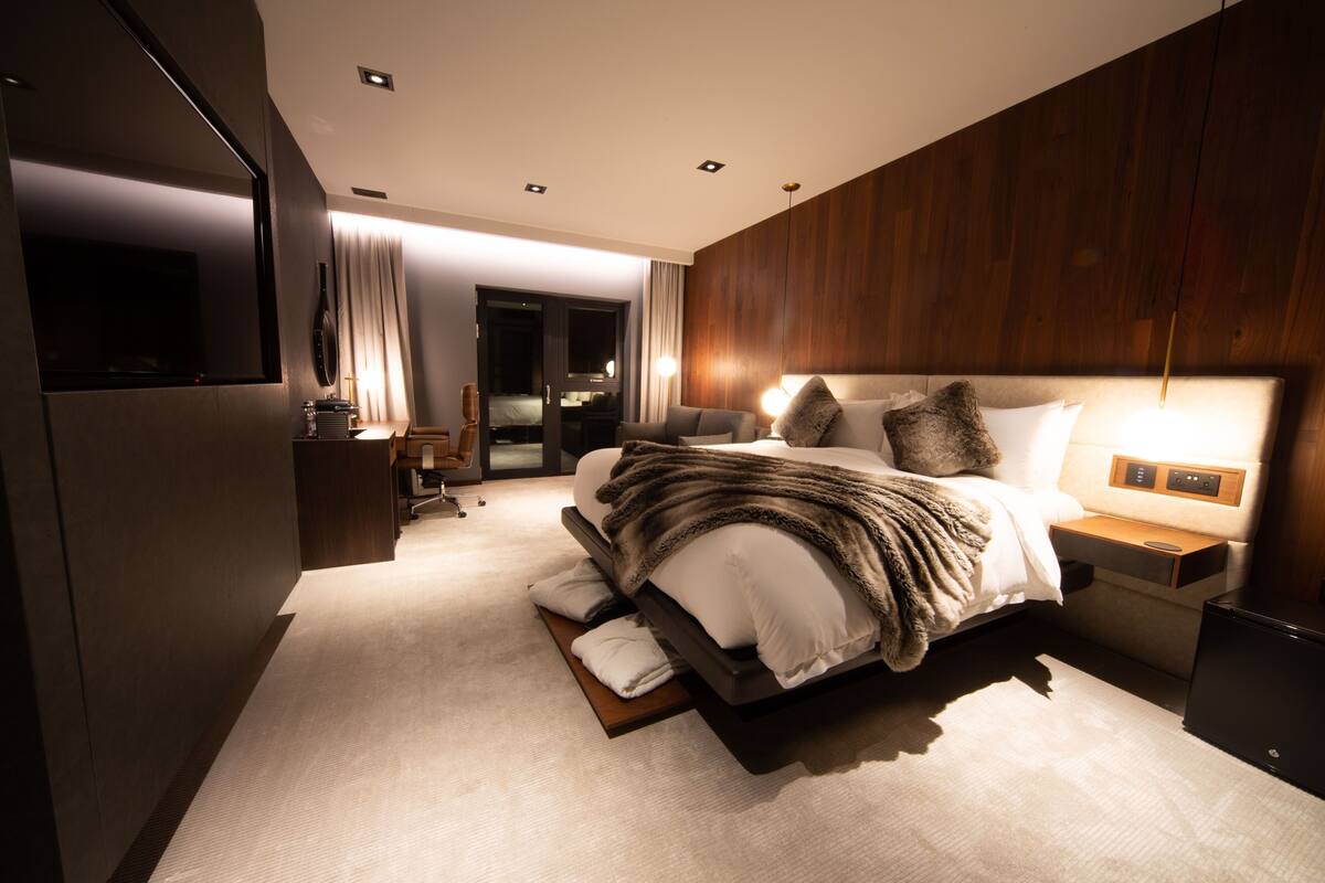 Quarto moderno com uma cama grande, mesas de cabeceira, uma TV e cabeceira de madeira.