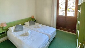 Uma cama de casal com lençóis brancos, cabeceira verde e uma pequena mesa de cabeceira com abajur.