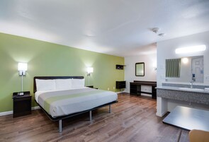 Quarto de hotel com cama, mesas de cabeceira, escrivaninha, cadeira, espelho e banheiro com pia e espelho.