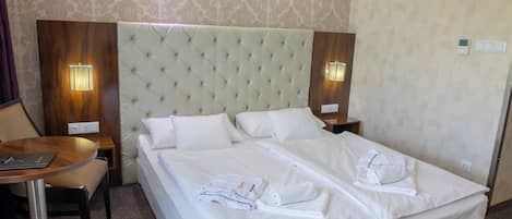 Quarto de hotel com uma cama grande, duas mesas de cabeceira, uma escrivaninha e uma cadeira.