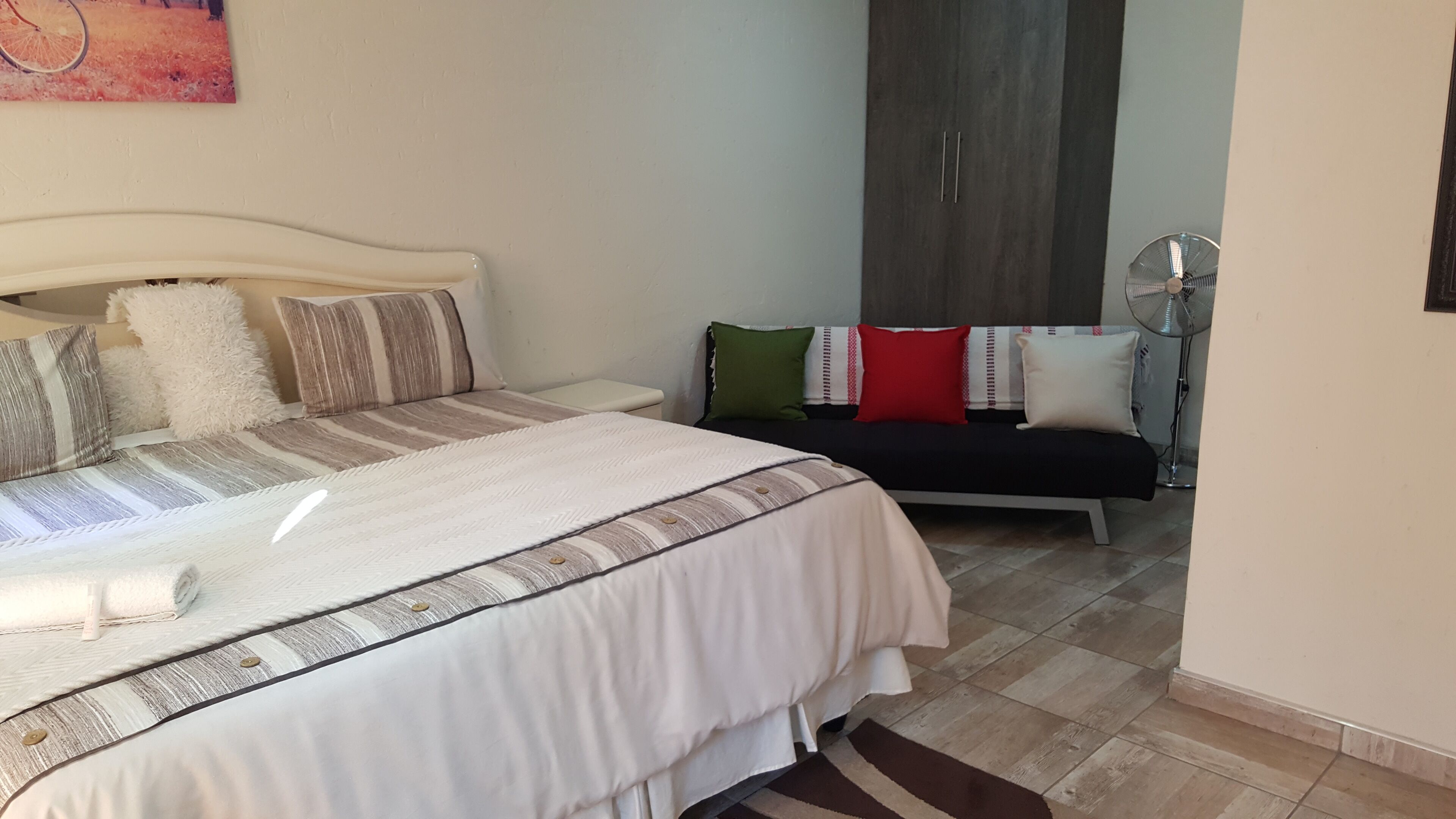 Quarto com cama, sofá, um ventilador e um quadro na parede.
