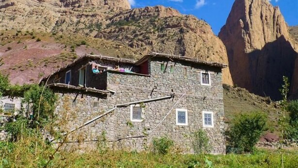 Um edifício de pedra com varanda, com montanhas ao fundo.