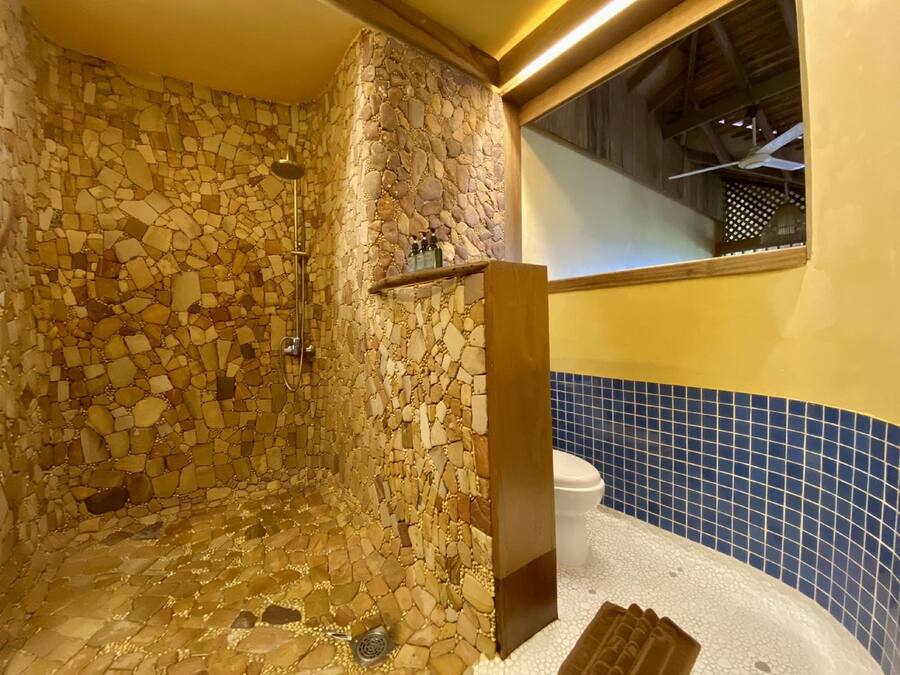 Um chuveiro com paredes de pedra e prateleira embutida, vaso sanitário branco e parede revestida em azulejos azuis.