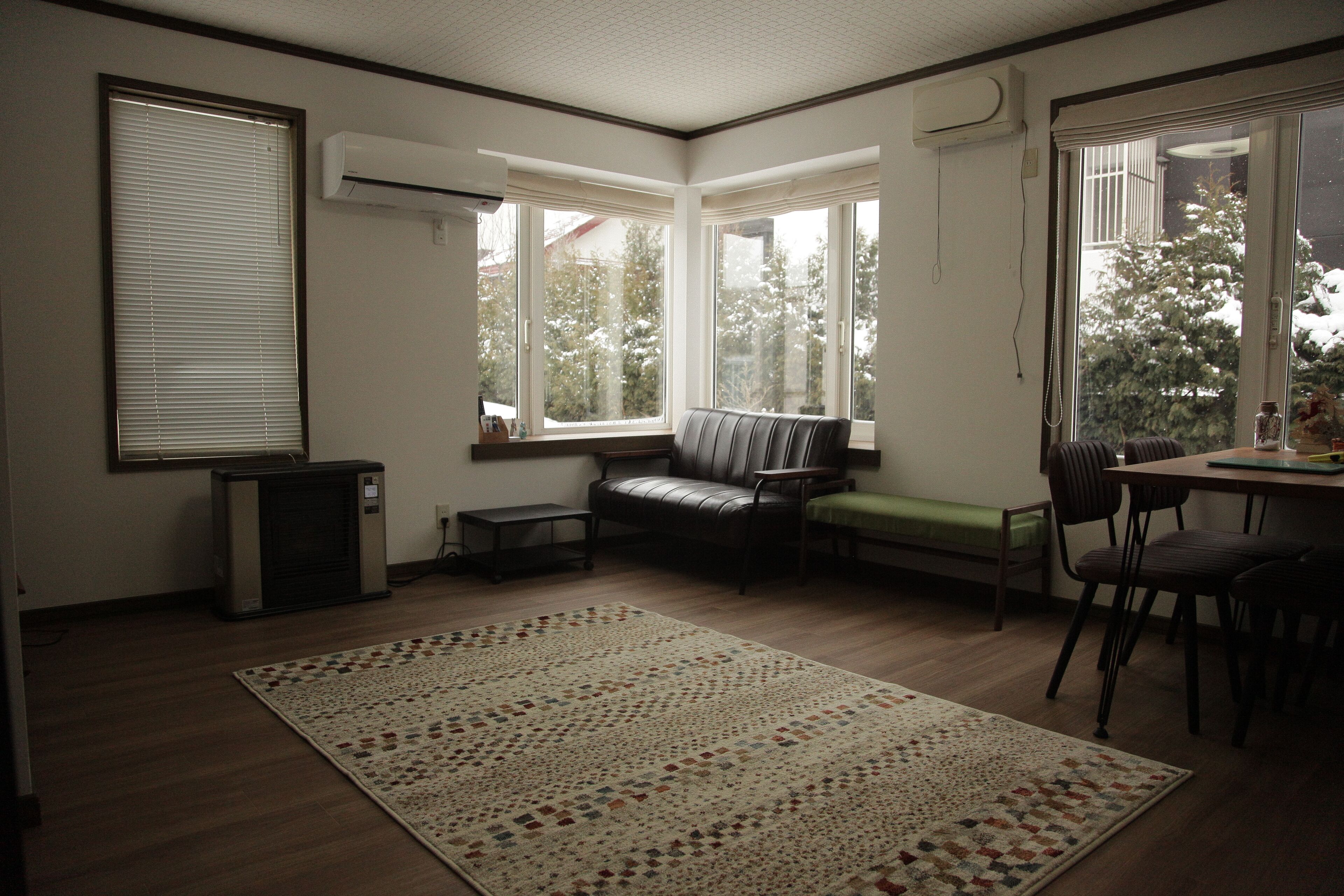 Um quarto com uma janela grande, um banco, uma mesa e uma cadeira.