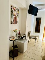 Uma sala de estar moderna com uma mesa de centro de vidro, uma geladeira branca, uma TV na parede, um quadro de flores e uma cadeira.