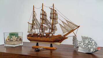Um modelo de navio de madeira sobre uma superfície de madeira, um recipiente de vidro com conchas e um objeto em formato de peixe.