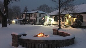 Paisagem coberta de neve com uma fogueira em primeiro plano, rodeada por montes de neve.