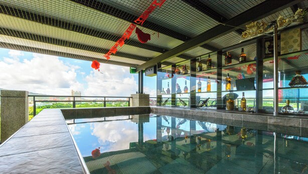 Piscina interior moderna com piso de vidro, área de bar com garrafas e vista para a paisagem urbana.